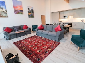 Uma sala de estar moderna com dois sofás cinzas, almofadas vermelhas, um tapete vermelho estampado e uma área de jantar com uma mesa e cadeiras de madeira.