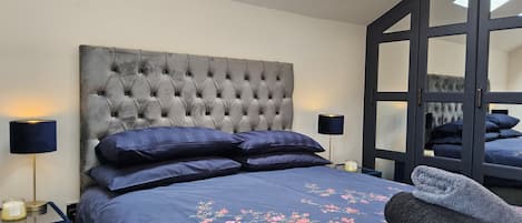 Quarto com cabeceira estofada, colcha florida e um claraboia acima da cama.