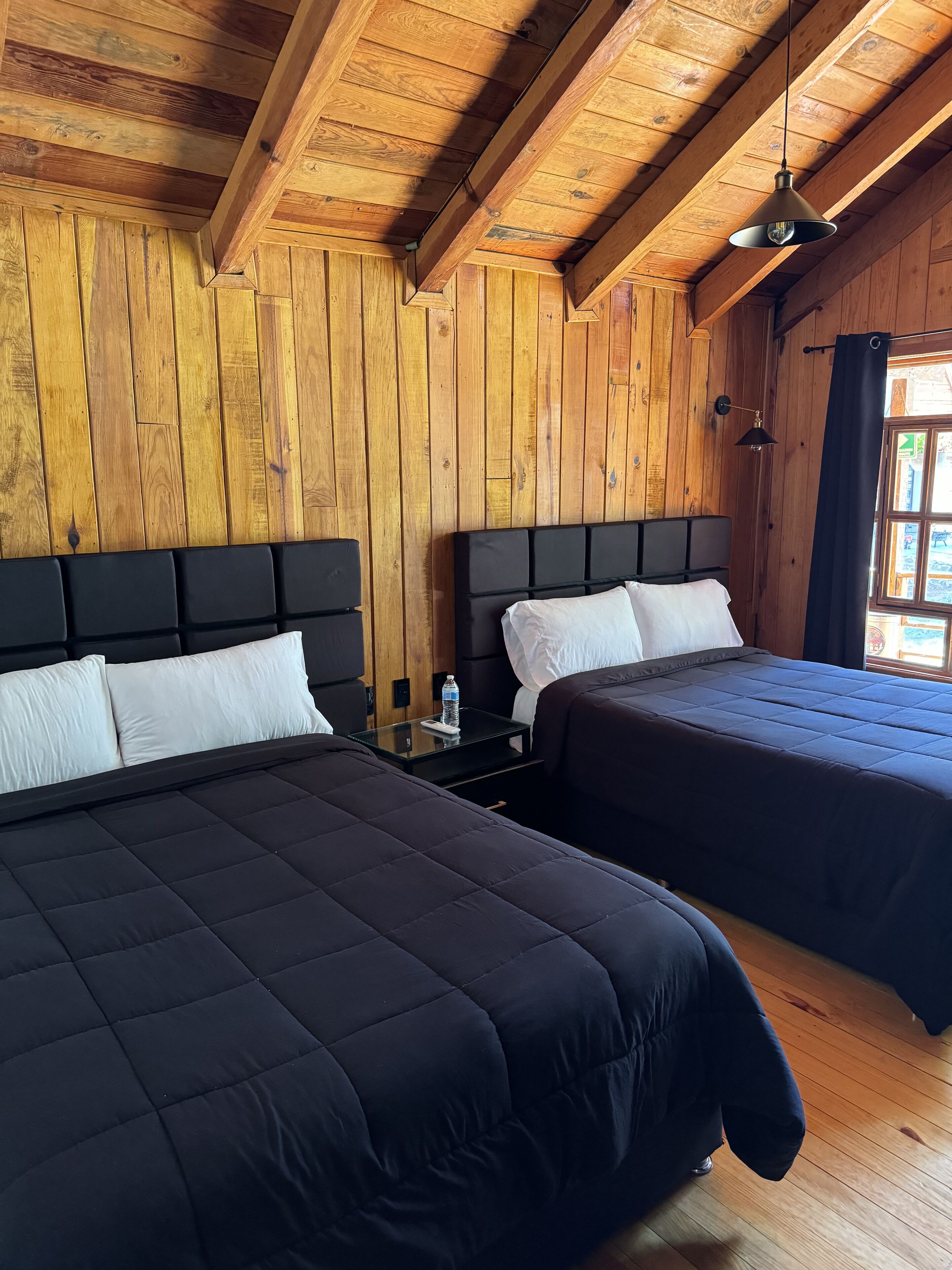 Quarto com painéis de madeira, duas camas, cada uma com cabeceira preta e roupa de cama branca.