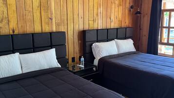 Quarto com painéis de madeira, duas camas, cada uma com cabeceira preta e roupa de cama branca.