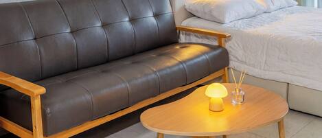 Quarto moderno com sofá de couro, mesa de centro de madeira com abajur e cama com roupa de cama branca.