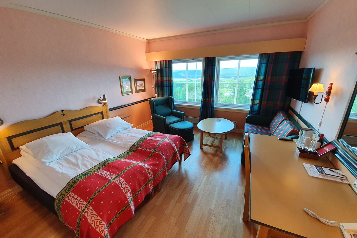 Quarto de hotel com cama, escrivaninha, cadeira, mesa pequena e sofá.