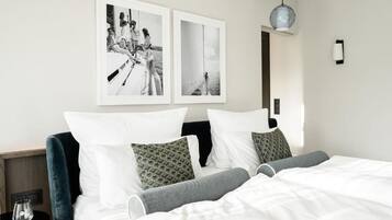 Uma cama bem arrumada com lençóis brancos e almofadas estampadas, uma cabeceira azul escura e duas fotografias preto e branco na parede.