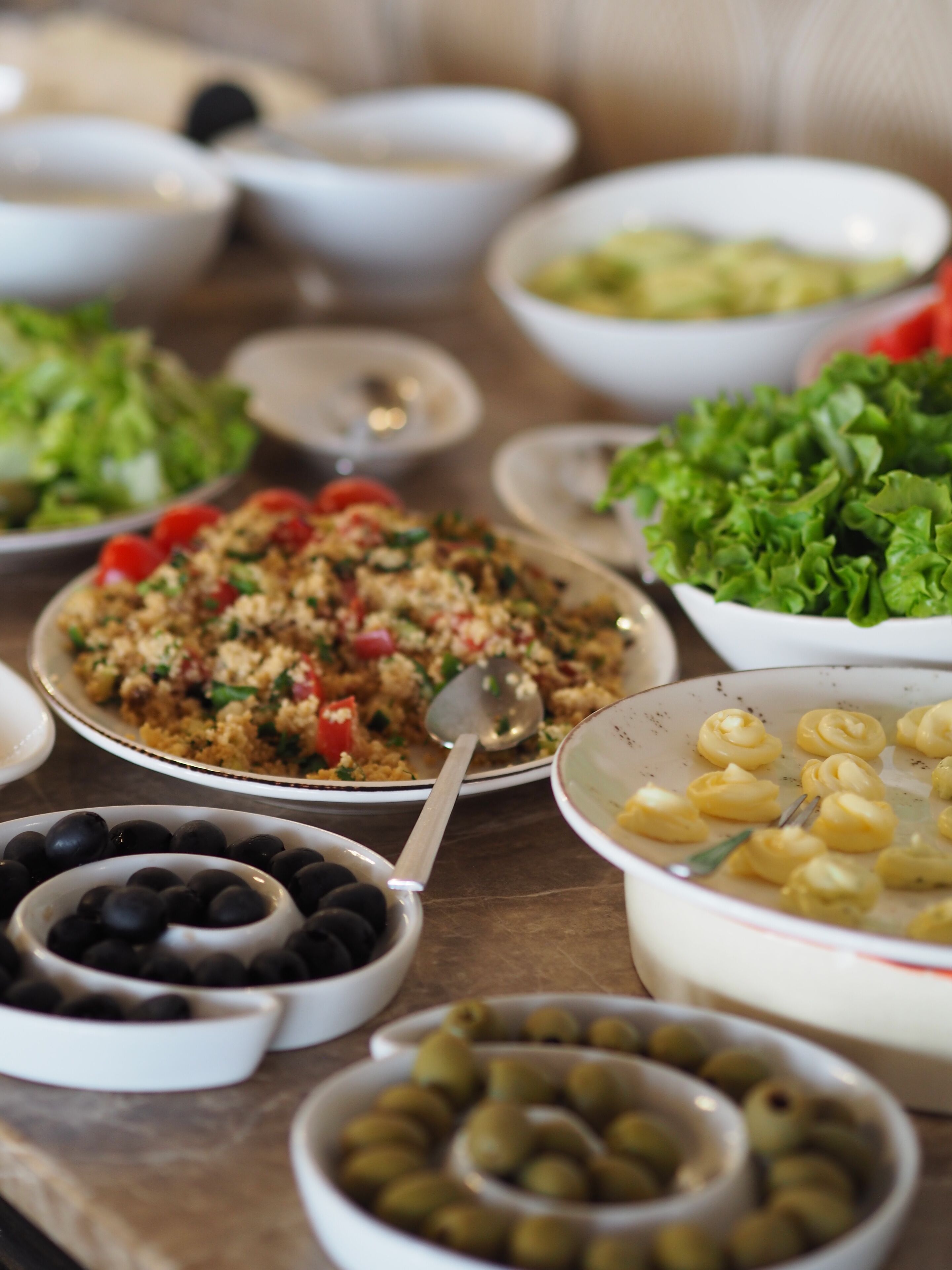Uma mesa com vários pratos, incluindo azeitonas, salada e um prato com uma colher.