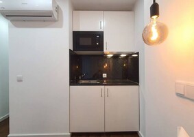 Cozinha compacta com armários brancos, bancada preta, micro-ondas e luminária pendente.