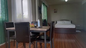 Quarto com cama, mesa de jantar com cadeiras, um ventilador e uma janela com cortinas.