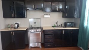 Uma cozinha compacta com armários escuros, um fogão de aço inoxidável, micro-ondas e pia.