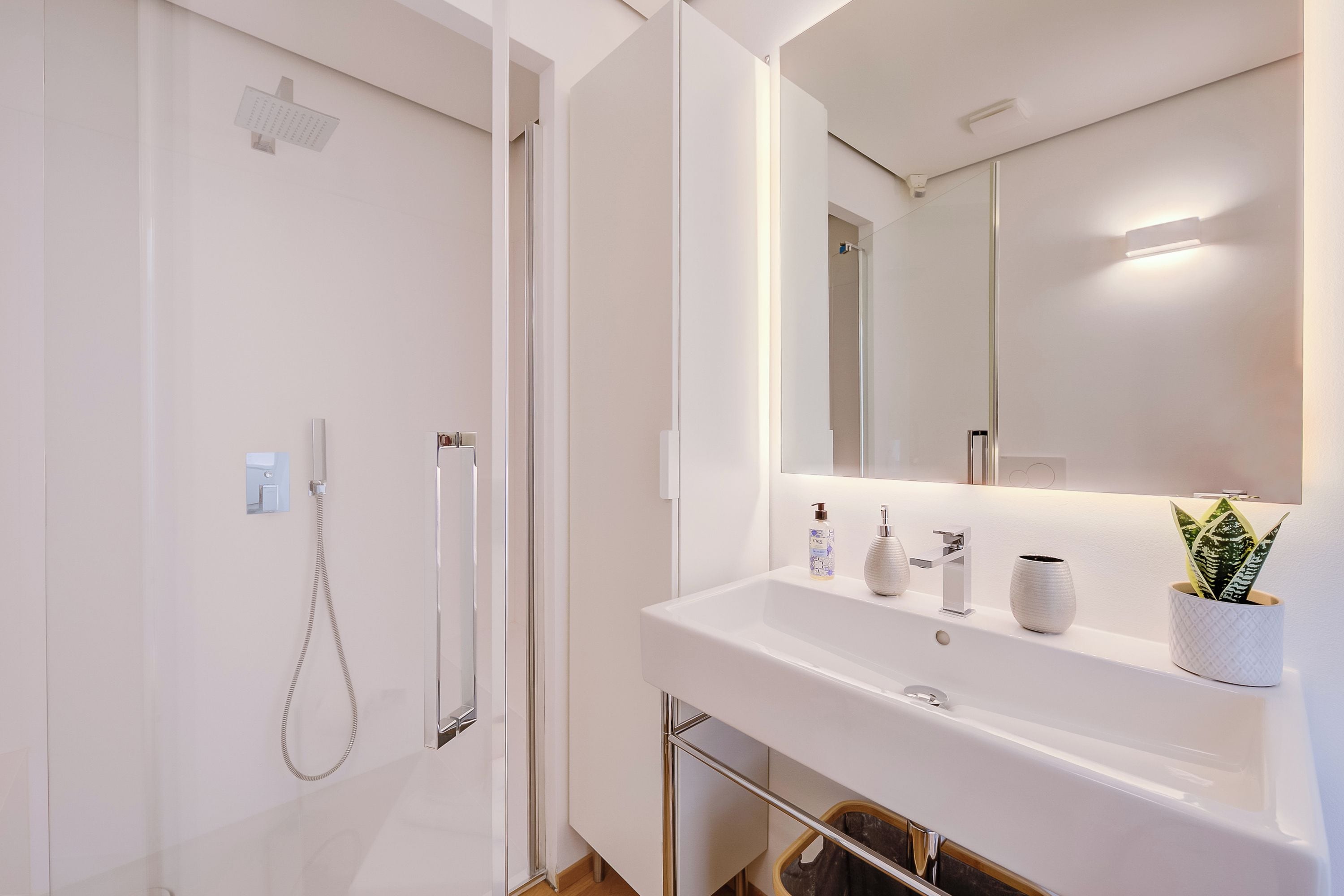 Casa de banho moderna com lavatório branco, espelho e chuveiro.