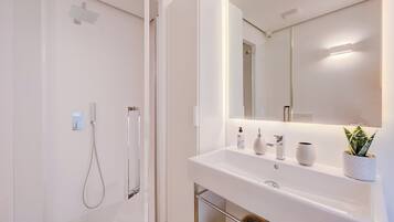 Casa de banho moderna com lavatório branco, espelho e chuveiro.
