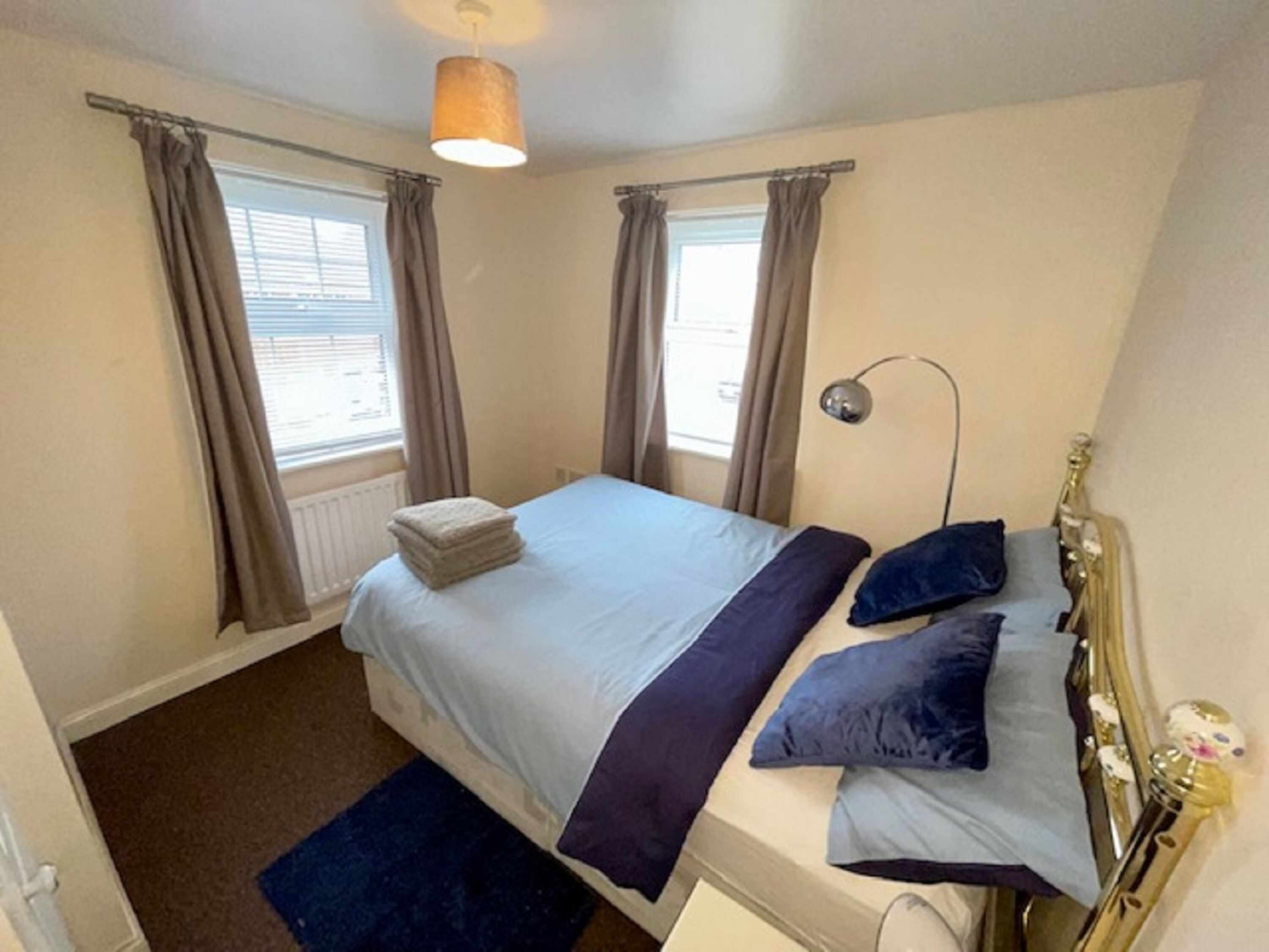 Quarto com cama, luminária de cabeceira, janela e radiador.
