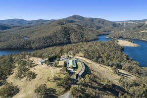 Vista aérea de um resort com um edifício curvo, rodeado por colinas arborizadas e um lago.