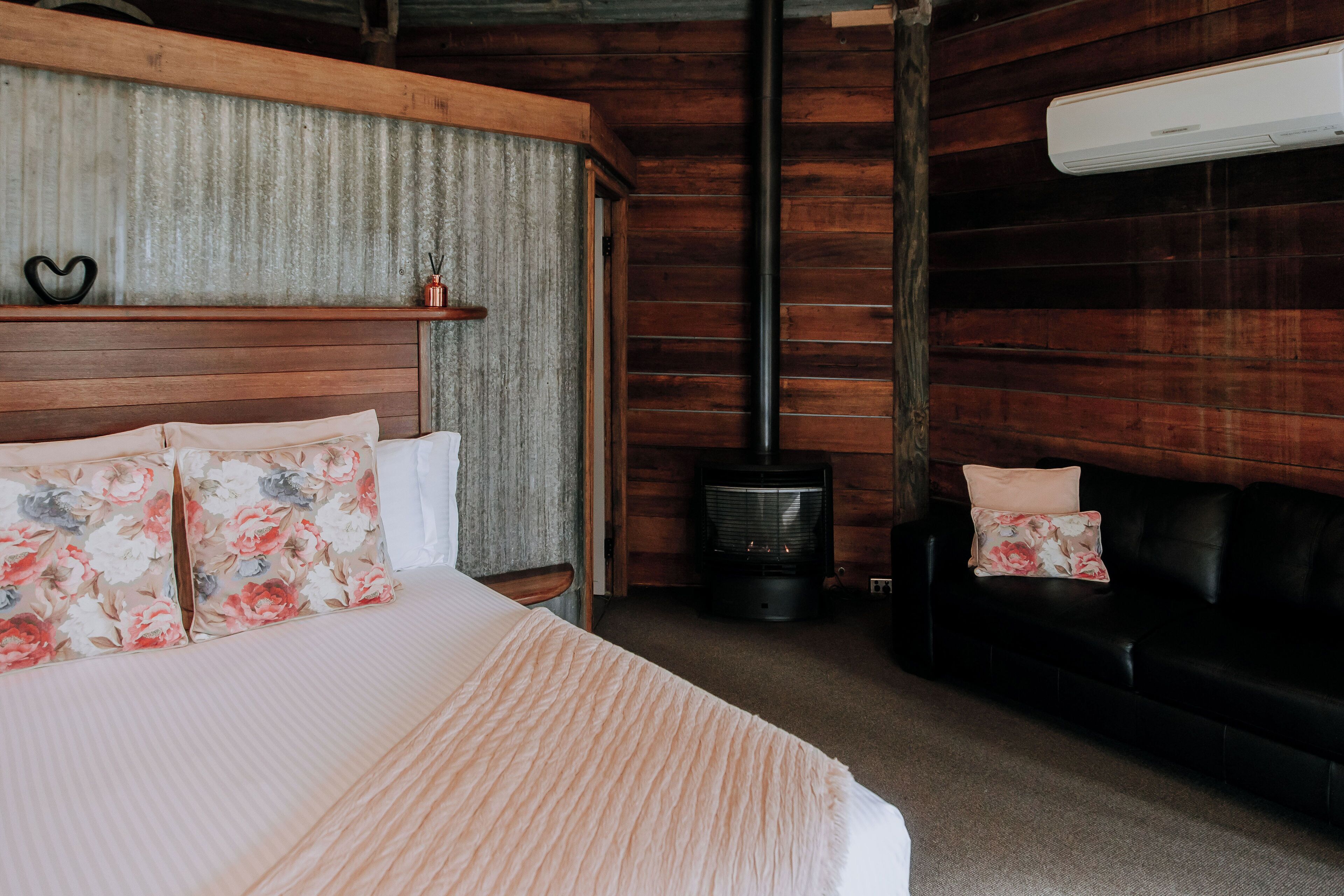 Quarto com cama, sofá de couro preto, lareira e parede de madeira.