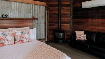 Quarto com cama, sofá de couro preto, lareira e parede de madeira.