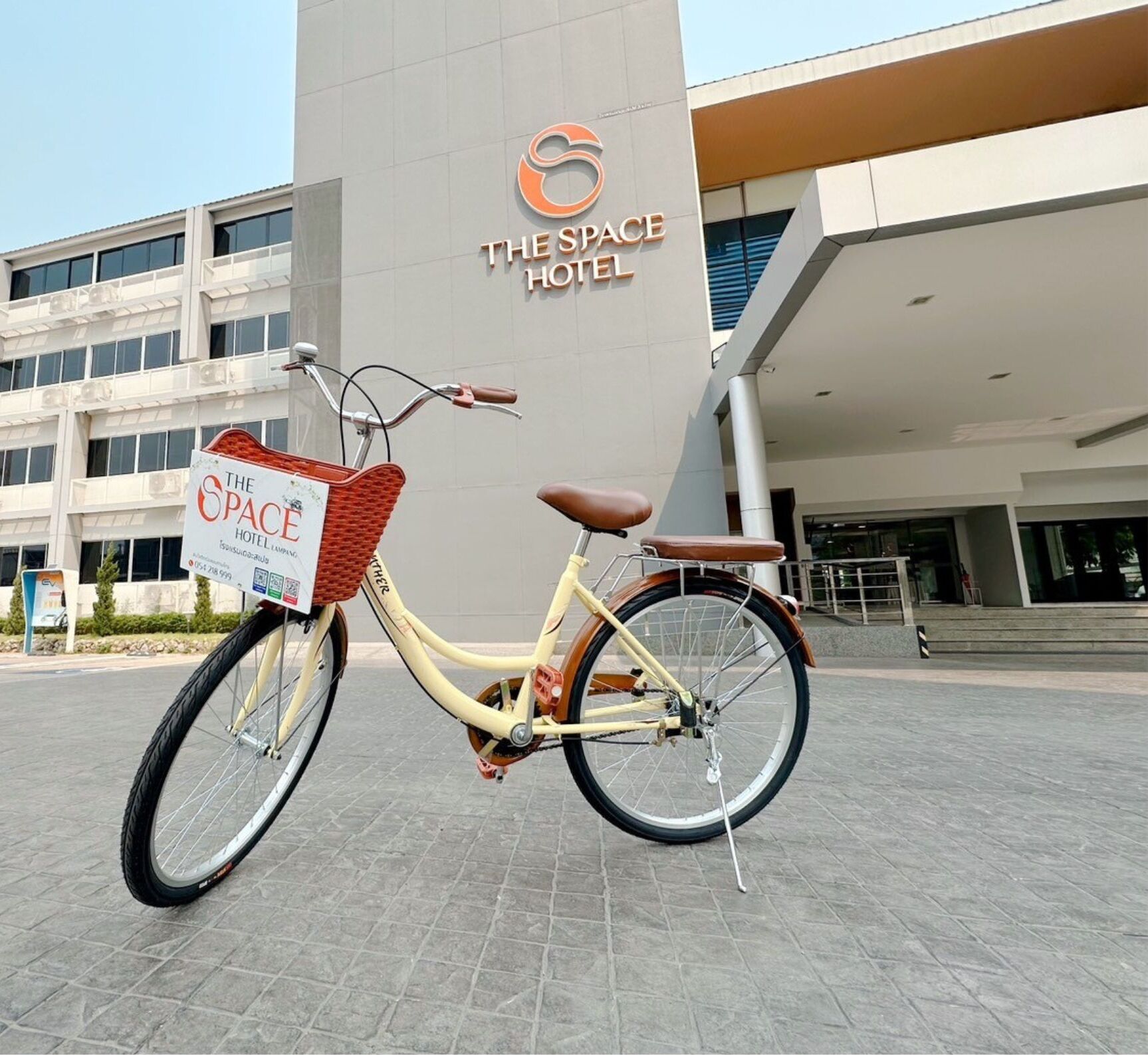 Uma bicicleta estacionada em frente ao The Space Hotel, com uma placa presa à cesta frontal.