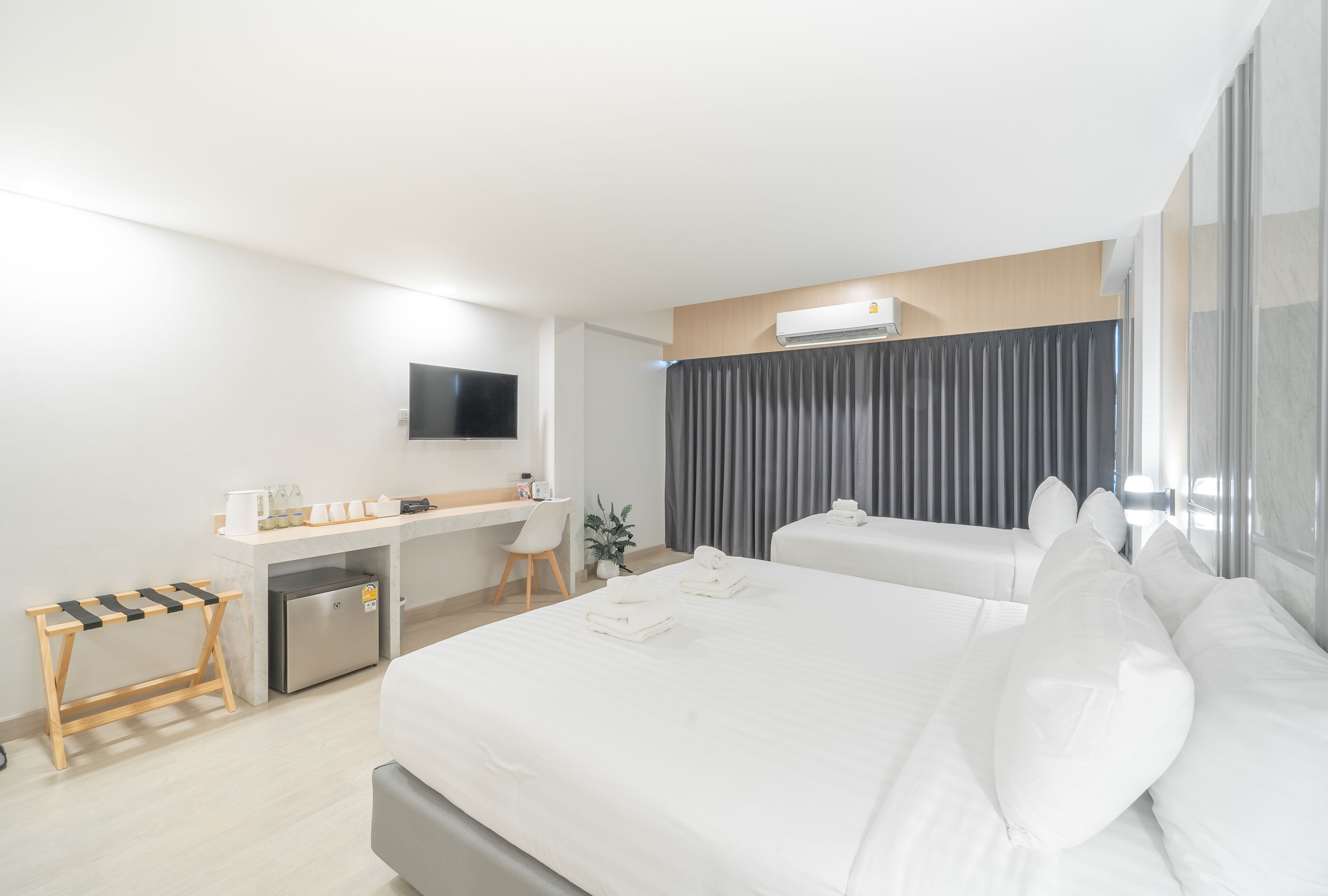 Quarto de hotel moderno com uma cama grande, uma escrivaninha com computador, um pequeno frigorífico e uma TV fixada na parede.