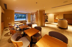 Interior de café moderno com mesas e cadeiras de madeira, um divisório de madeira decorativo e vista para o exterior através de grandes janelas.