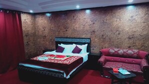 Quarto de hotel com uma cama grande, um sofá vermelho e uma pequena mesa.