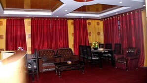 Quarto de hotel com carpete vermelho, um sofá, uma mesa de centro e uma área de jantar com cadeiras e mesa.