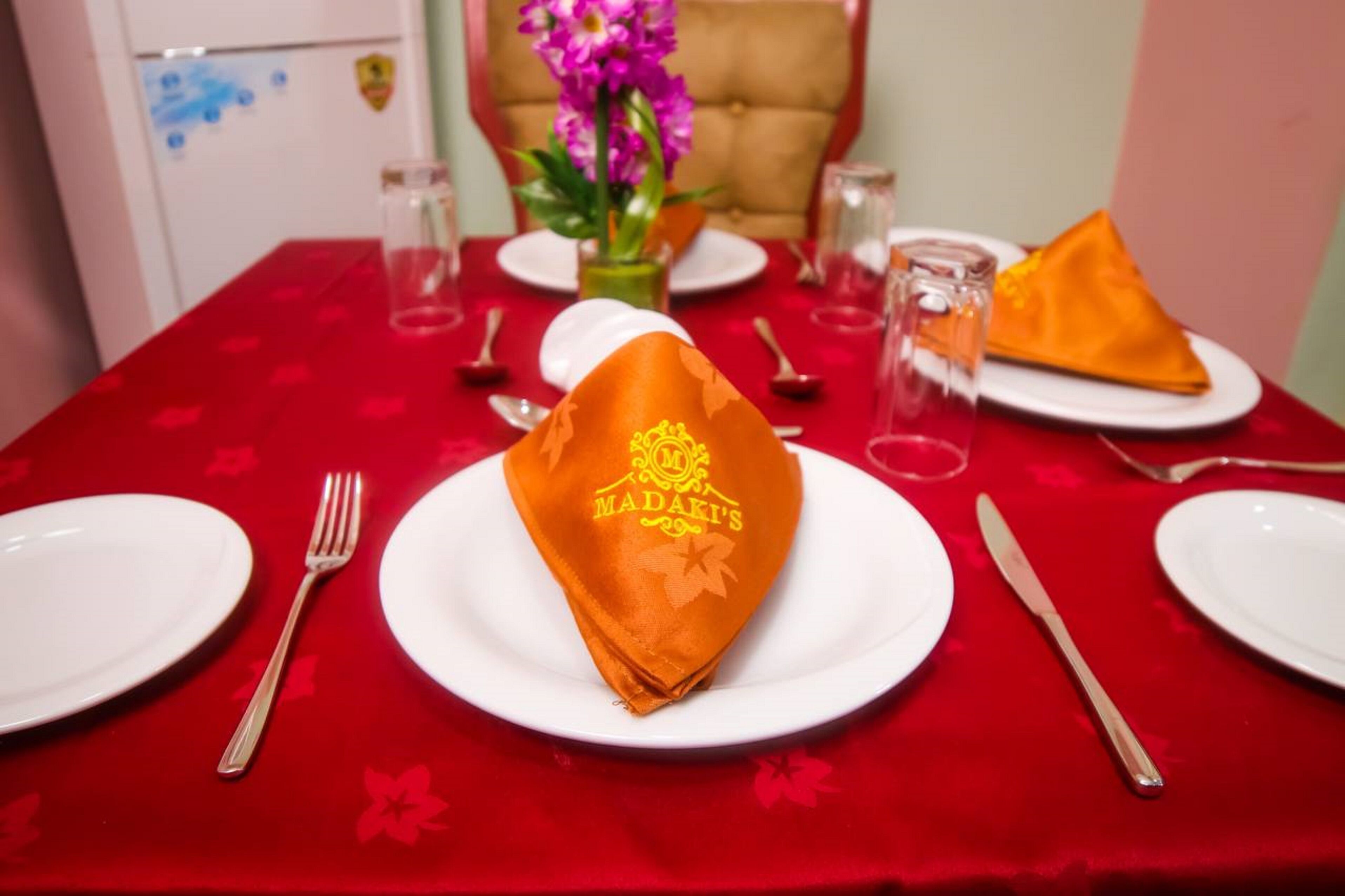 Mesa de jantar posta com pratos brancos, talheres e toalha de mesa vermelha.