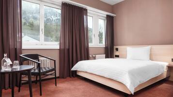 Quarto de hotel com cama, cadeira, mesa e janela com cortinas.