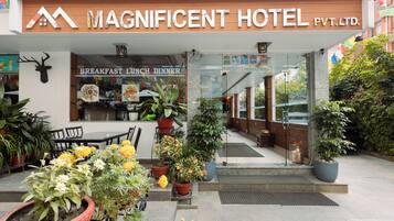 Exterior do Magnífico Hotel, com placa indicando café da manhã, almoço e jantar.
