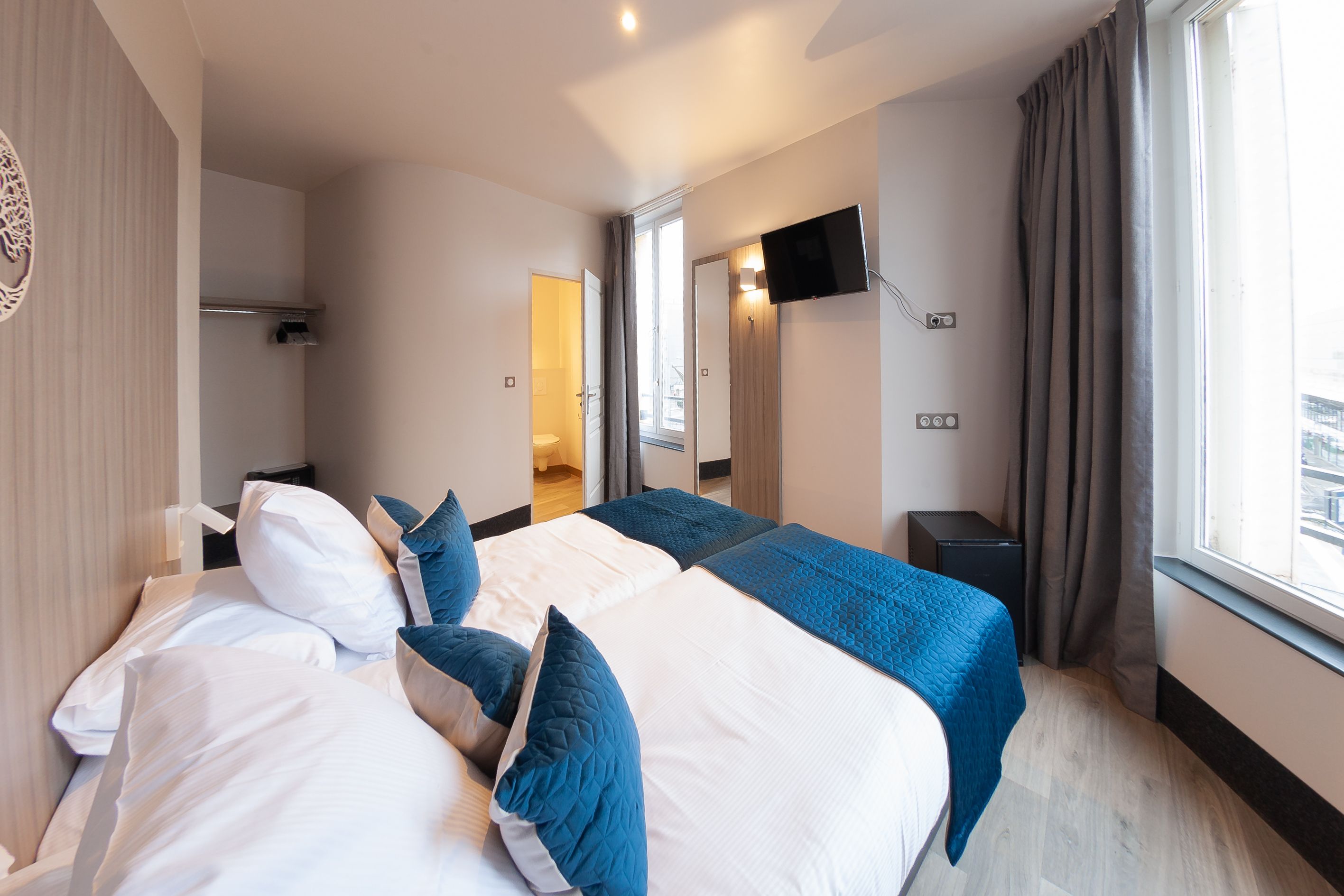 Quarto de hotel com uma cama grande, televisão de tela plana na parede e janela com cortinas.