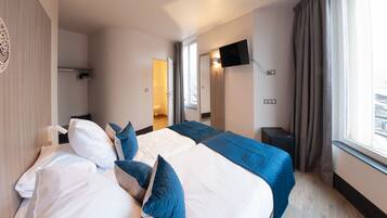 Quarto de hotel com uma cama grande, televisão de tela plana na parede e janela com cortinas.
