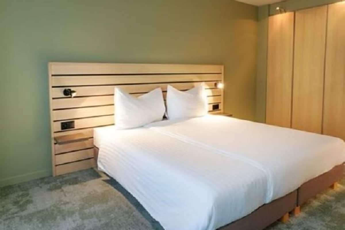 Cama bem arrumada com cabeceira de madeira e duas almofadas, mesa de cabeceira de madeira e guarda-roupa com espelho.