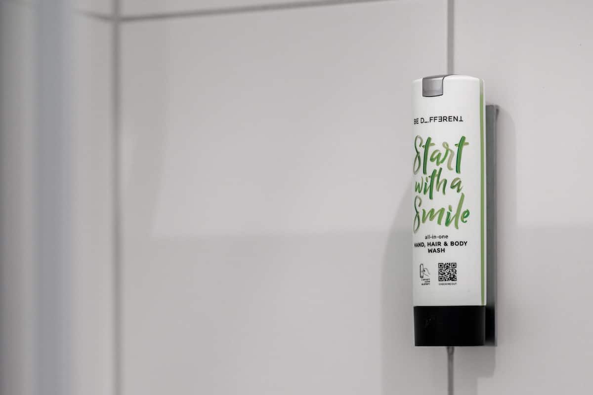 Um dispensador de álcool em gel fixado numa parede revestida de azulejos brancos.