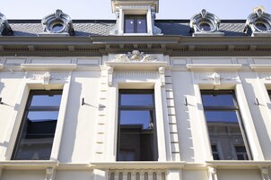 Fachada de edifício com três janelas grandes, molduras decorativas e design simétrico.