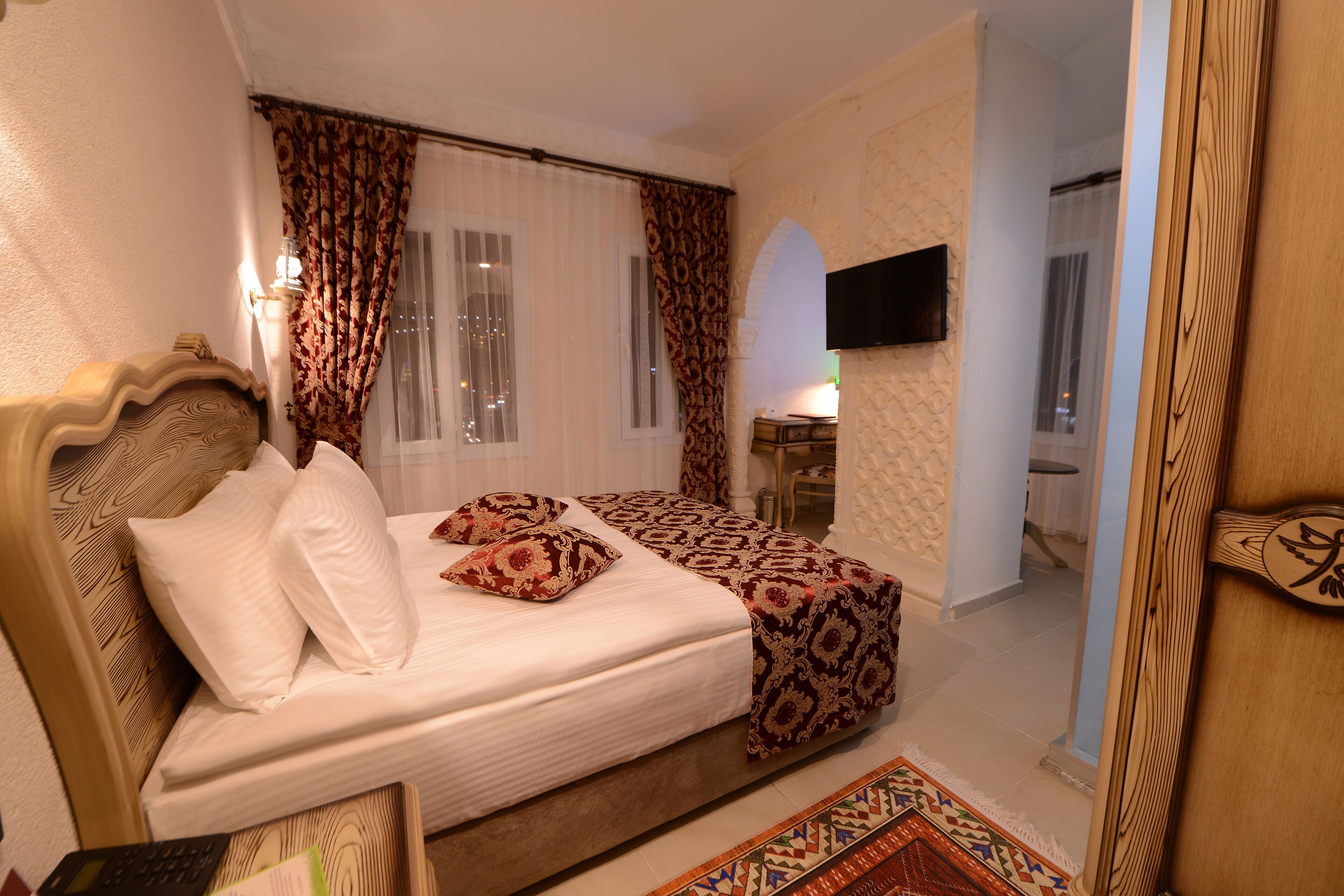 Quarto de hotel com cama, escrivaninha, televisão e vista para o exterior.