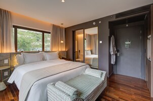 Quarto de hotel moderno com cama grande, mesa de cabeceira, espelho e vista para o exterior.