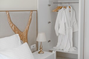 Quarto de hotel com cama, luminária de cabeceira, cabides com roupões e porta-toalhas na parede.