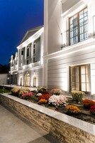 Um edifício grande e branco com fachada simétrica, várias janelas e um jardim bem cuidado com diversas flores.