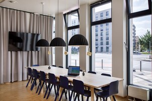 Uma sala de reunião moderna com uma mesa grande, cadeiras, um laptop e luminárias pendentes.