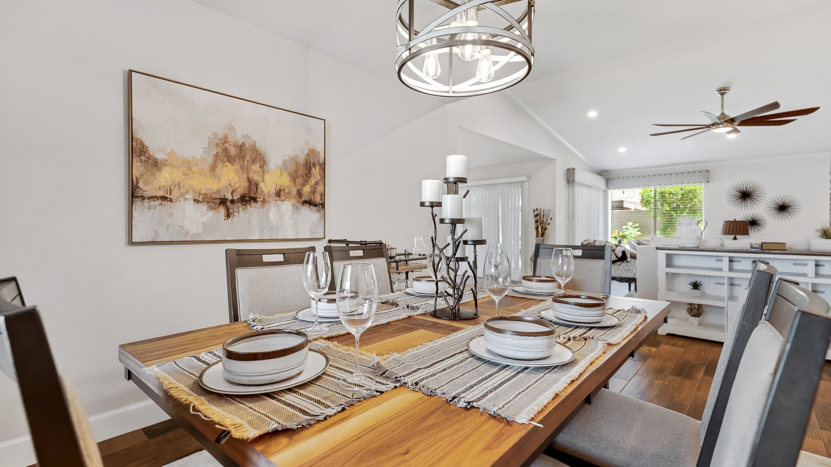 Uma área de refeições com mesa de madeira posta para quatro pessoas, rodeada por cadeiras.