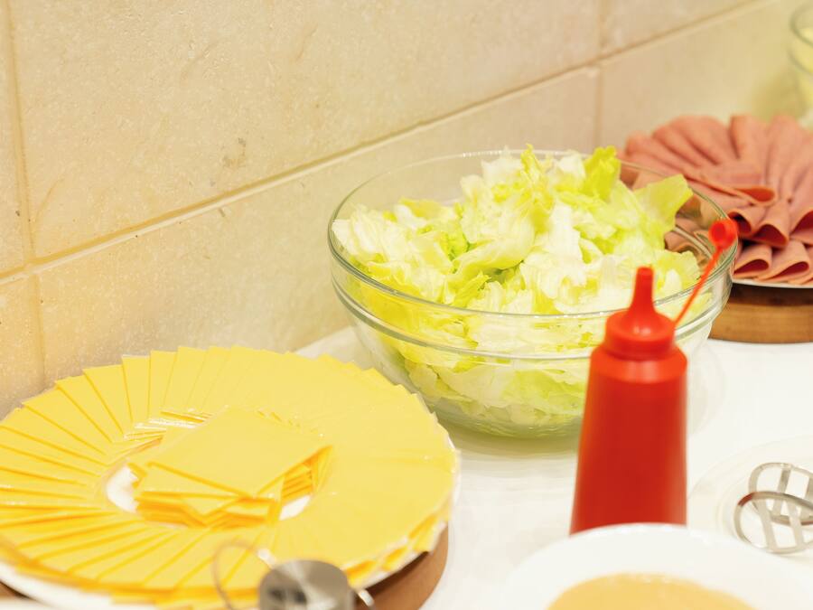 Uma mesa com um prato de comida amarela, uma salada e um frasco de molho vermelho, além de carne fatiada.