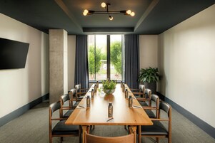 Uma sala de conferências com uma mesa comprida, cadeiras, uma planta e vista pela janela.