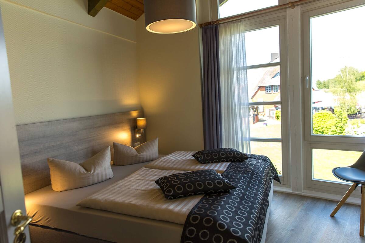 Quarto de hotel com uma cama grande, uma cadeira e vista para o exterior.