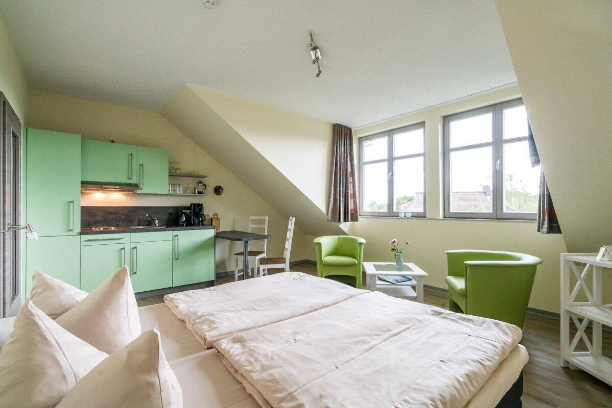 Quarto com cama, cozinha compacta, área de refeições e janela com cortinas.