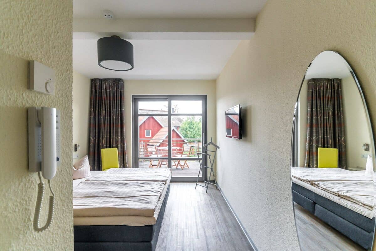 Quarto de hotel com cama, televisão, telefone e vista para um edifício vermelho lá fora.