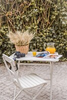 Uma mesa branca com uma câmera, uma cesta de plantas secas, um copo de suco de laranja e uma revista.