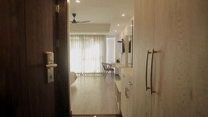 Um corredor que leva a um quarto com ventoinha no teto, janela com cortinas e televisão de tela plana na parede.