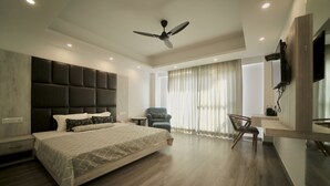 Quarto moderno com cama grande, ventilador de teto, televisão na parede e janela com cortinas.