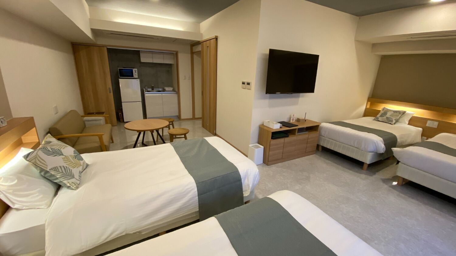 Quarto de hotel com duas camas, televisão, secretária e cozinha compacta.