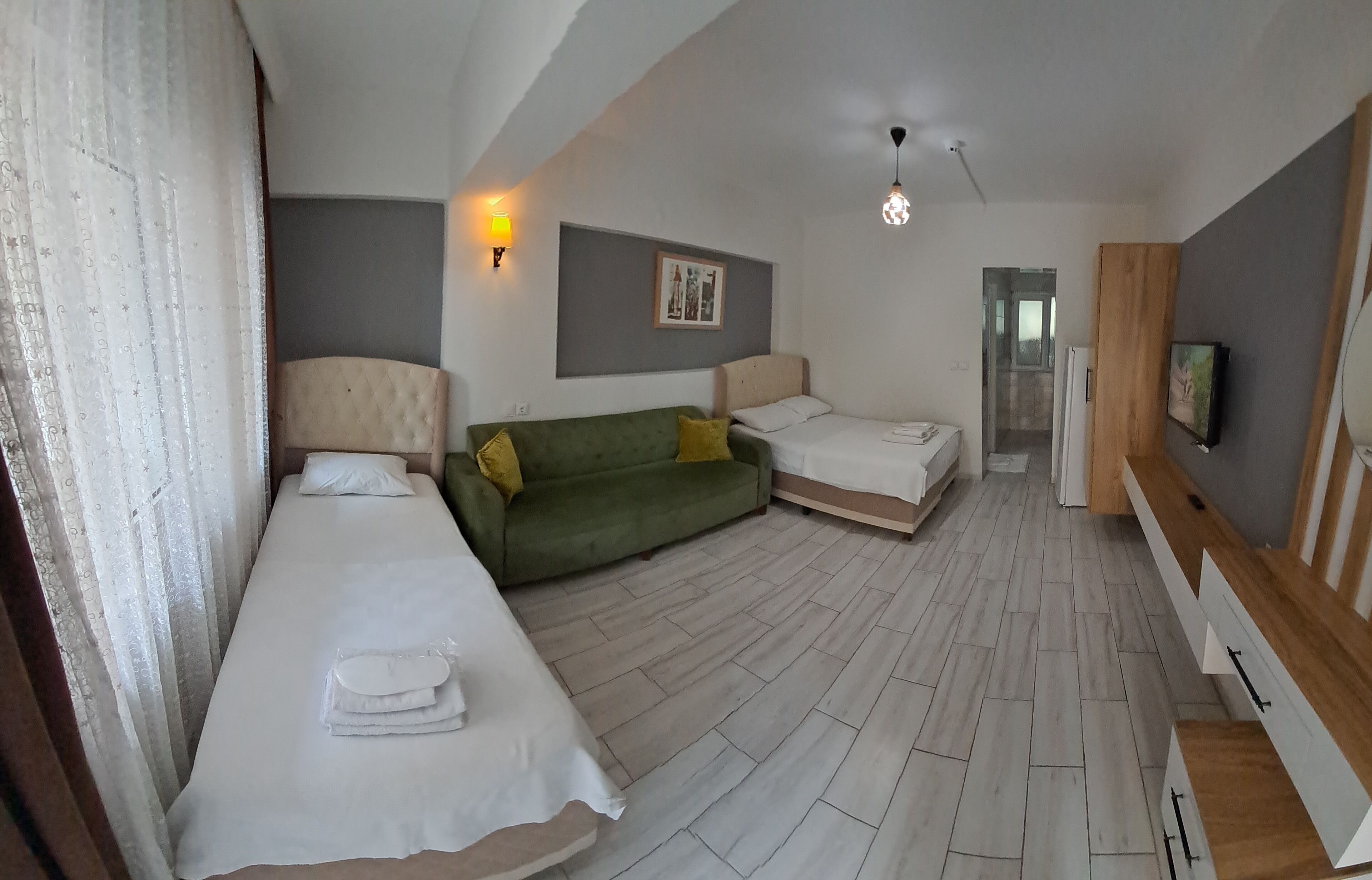 Quarto de hotel com duas camas, um sofá verde, um banco de madeira, uma televisão e um quadro na parede.