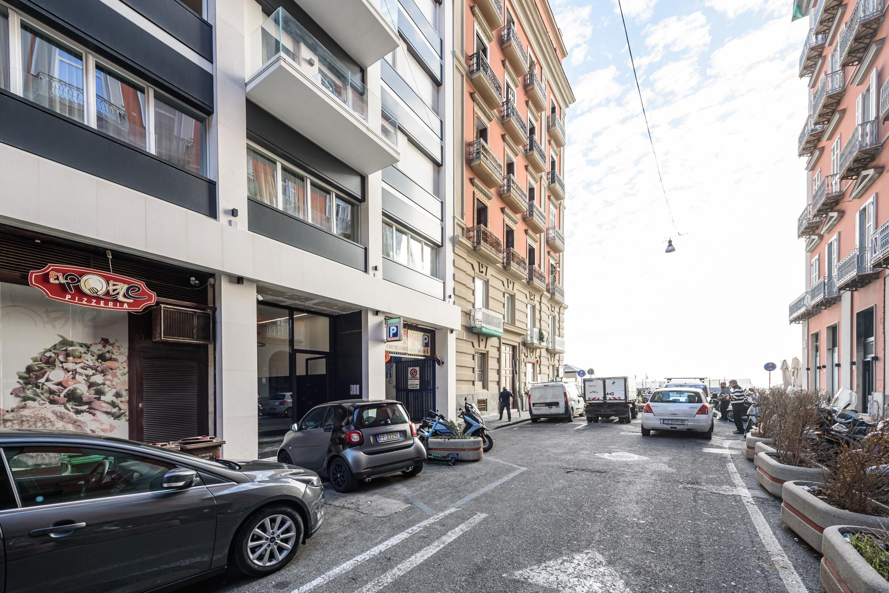 Rua com carros estacionados, pizzaria e edifícios altos.