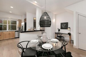 Uma cozinha moderna com armários de madeira, uma ilha central e um espaço de jantar com mesa de vidro e cadeiras pretas.