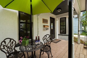 Um alpendre coberto com mesa e cadeiras, um guarda-sol verde e uma porta com caixa de correio.