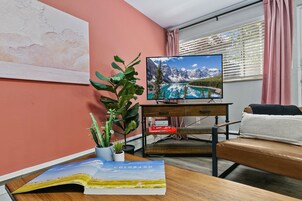 Uma sala de estar com televisão exibindo uma paisagem de montanhas, uma planta de cacto, um livro intitulado 'Colorado Atlas' e um sofá.